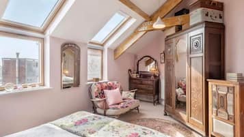 Quarto com claraboia, cama com roupa de cama florida, cómoda e cadeira com almofada floral.