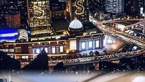 Paisagem urbana noturna com edifícios iluminados e um símbolo de dólar em destaque.