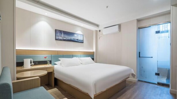 Quarto de hotel moderno com uma cama grande, uma mesinha de cabeceira, uma cadeira e um quadro na parede.