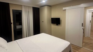Quarto de hotel com uma cama grande, uma televisão de tela plana na parede, uma porta com puxador e uma luminária no teto.