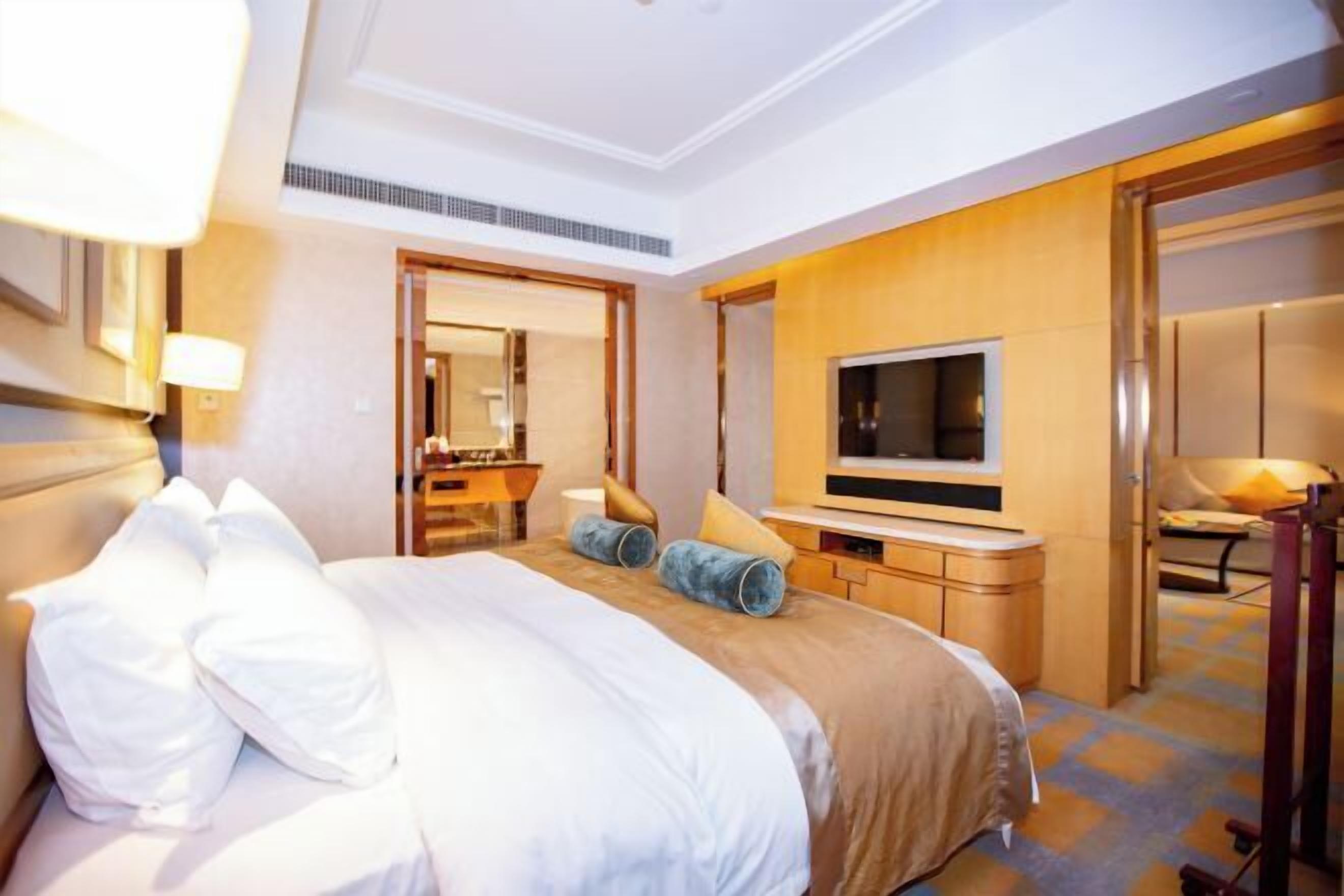 Quarto de hotel com uma cama grande, televisão, escrivaninha e espelho.