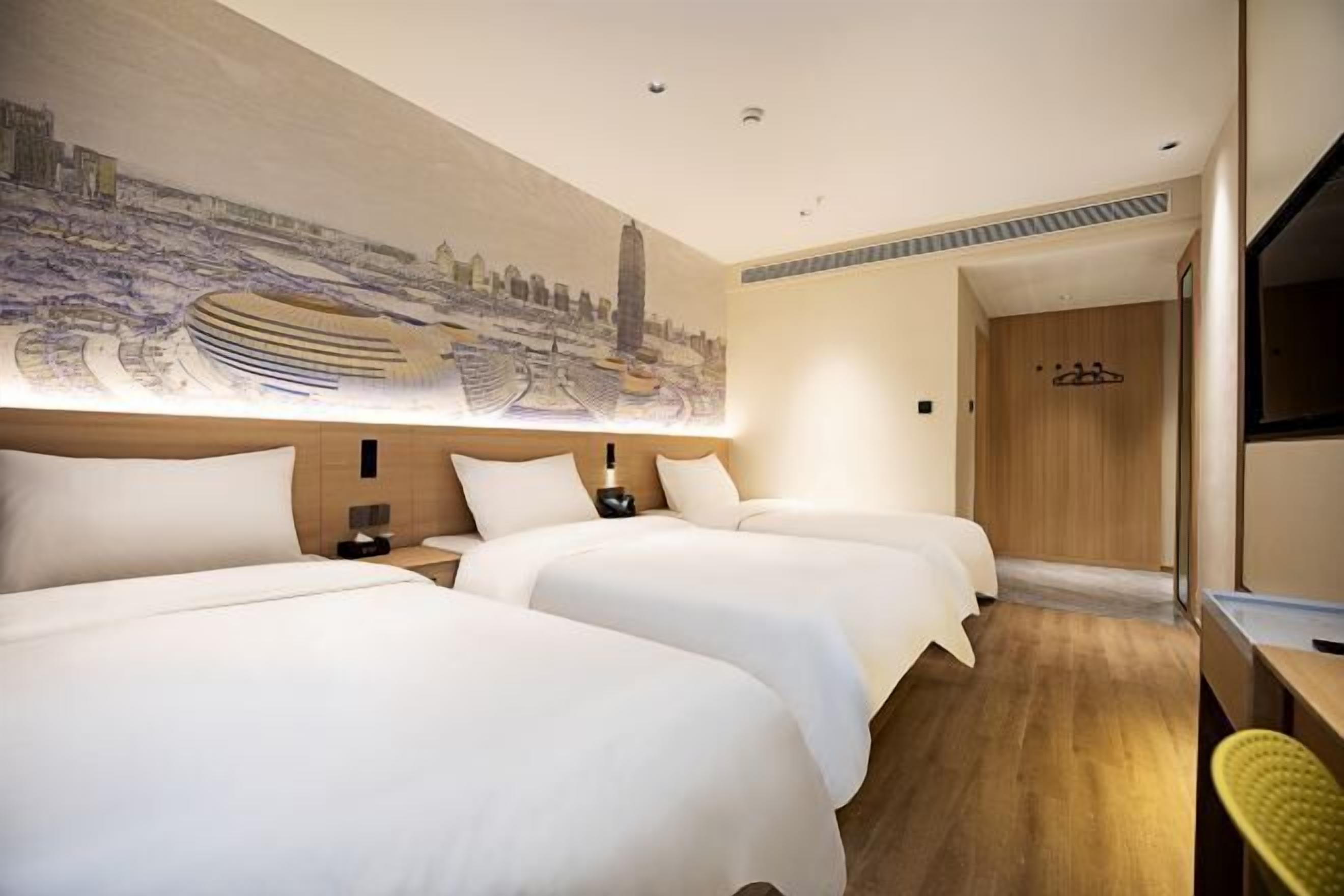 Quarto de hotel com duas camas, um mural na parede, piso de madeira e uma escrivaninha com uma cadeira.