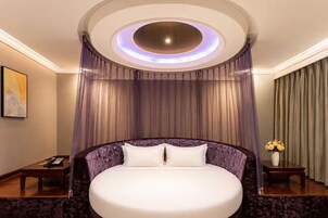 Quarto de hotel moderno com uma cama grande, uma luminária redonda no teto e vista para a cidade.
