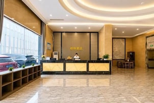 Uma área de recepção de hotel com piso de mármore, balcão de atendimento, um recepcionista e vista para carros estacionados lá fora.