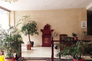 Um hall de entrada com balcão de recepção, peça decorativa vermelha e plantas em vasos.