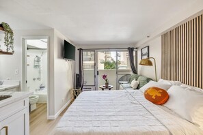 Quarto moderno com cama, televisão, varanda e banheiro.