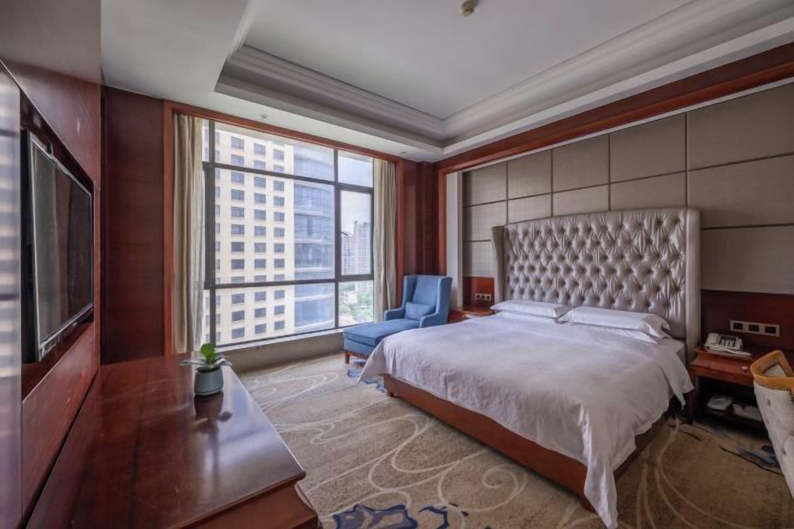 Quarto de hotel com uma cama grande, televisão, escrivaninha, cadeira e janela com vista para a cidade.