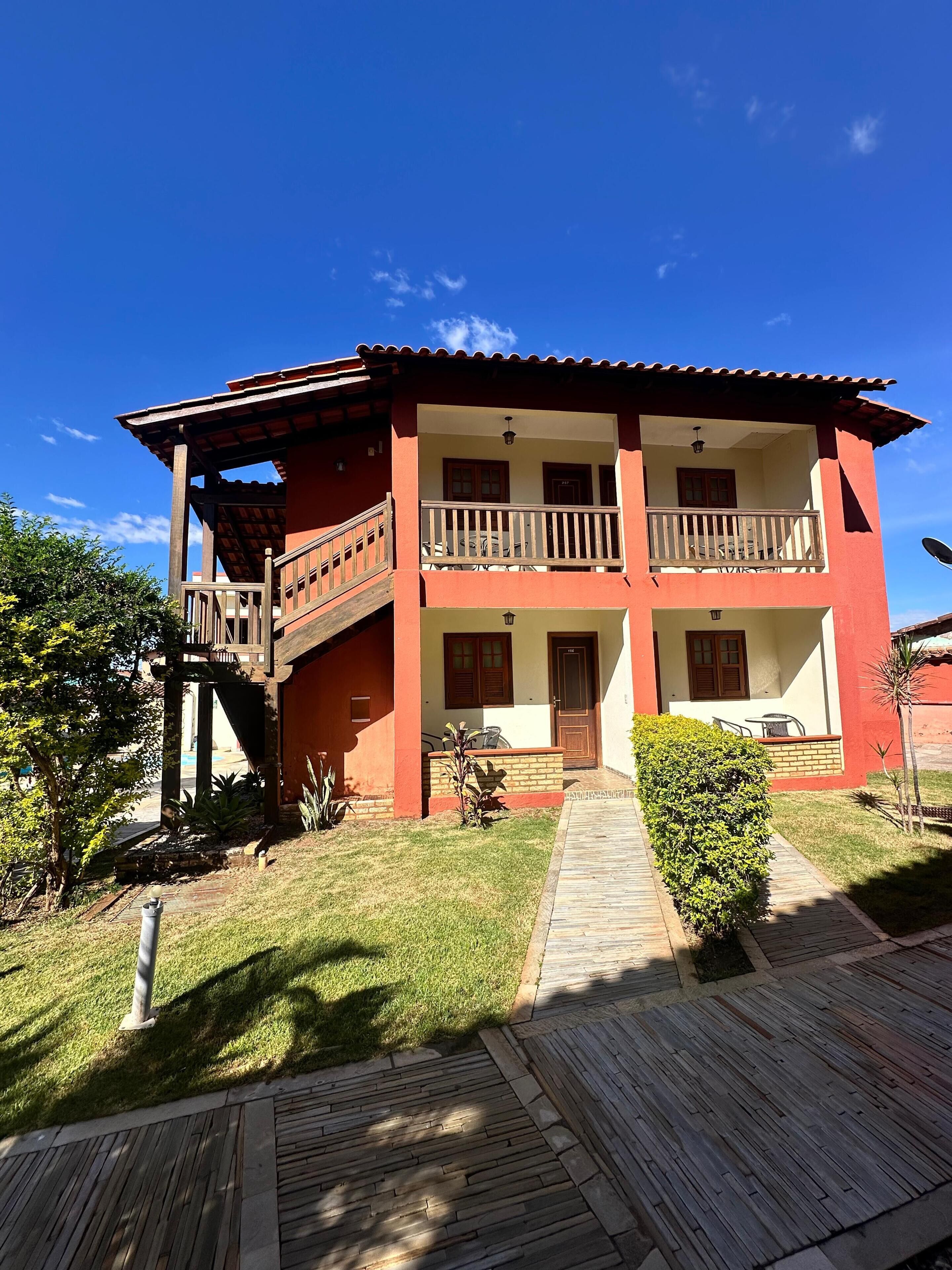 Um edifício de dois andares com varanda, deck de madeira e gramado bem cuidado.