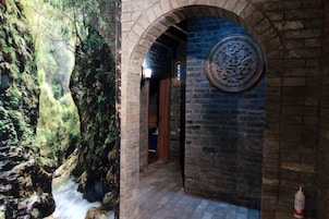 Um corredor de tijolos em arco com decoração circular na parede e vista para área externa rochosa.