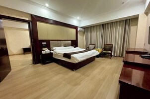 Quarto de hotel com cama de casal, escrivaninha, cadeira, guarda-roupa e um espelho grande.