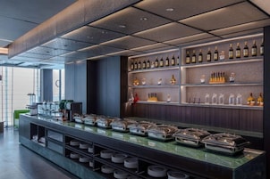 Uma área de bar com um balcão comprido, prateleiras com garrafas e pratos e copos organizados.