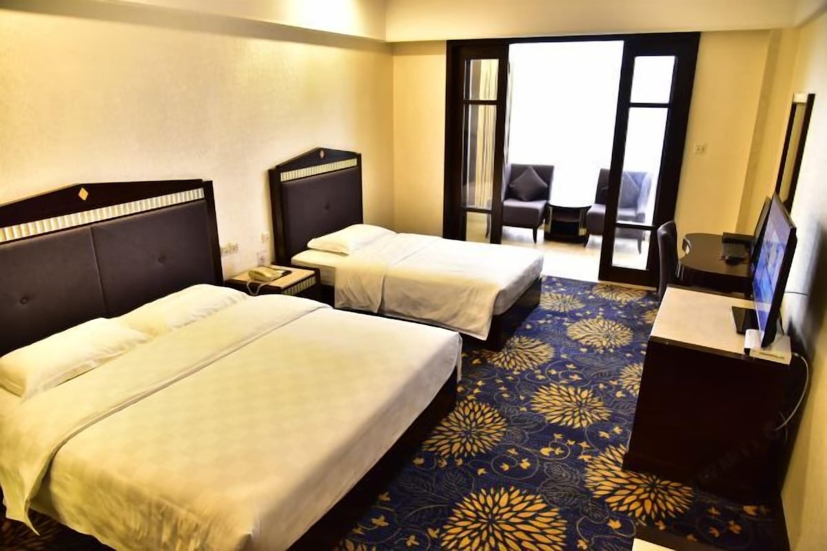 Quarto de hotel com duas camas, uma escrivaninha, televisão e porta para uma varanda.