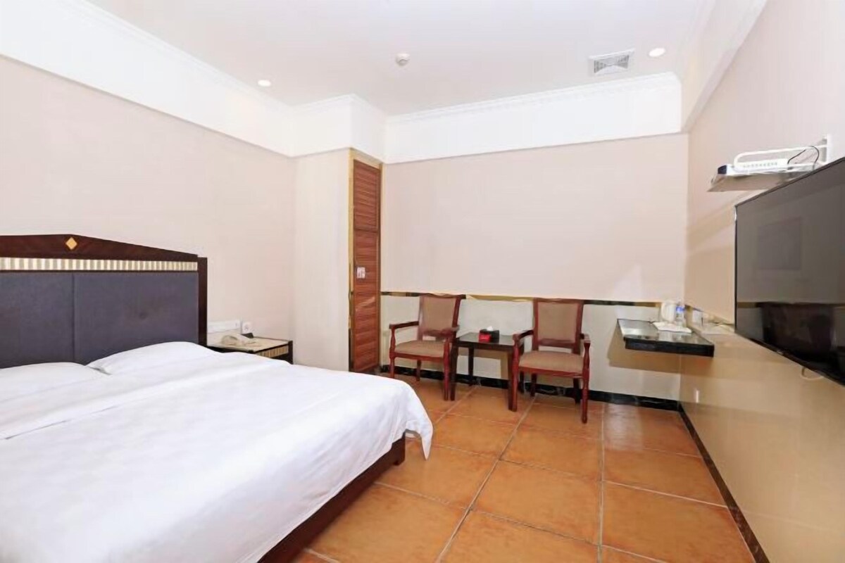 Quarto de hotel com cama, escrivaninha, duas cadeiras, televisão e uma mesinha.