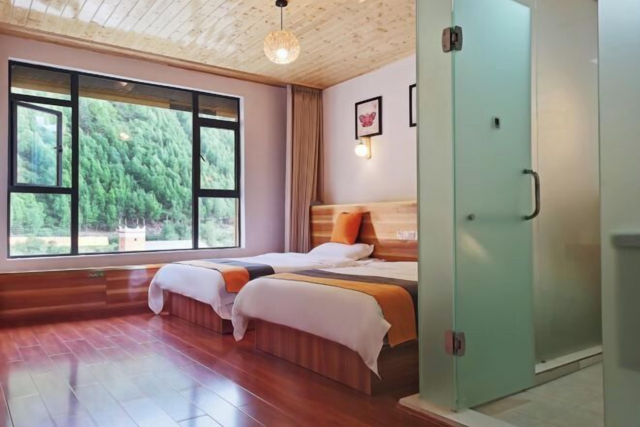 Quarto com duas camas, janelas amplas, teto de madeira e porta de vidro para o chuveiro.