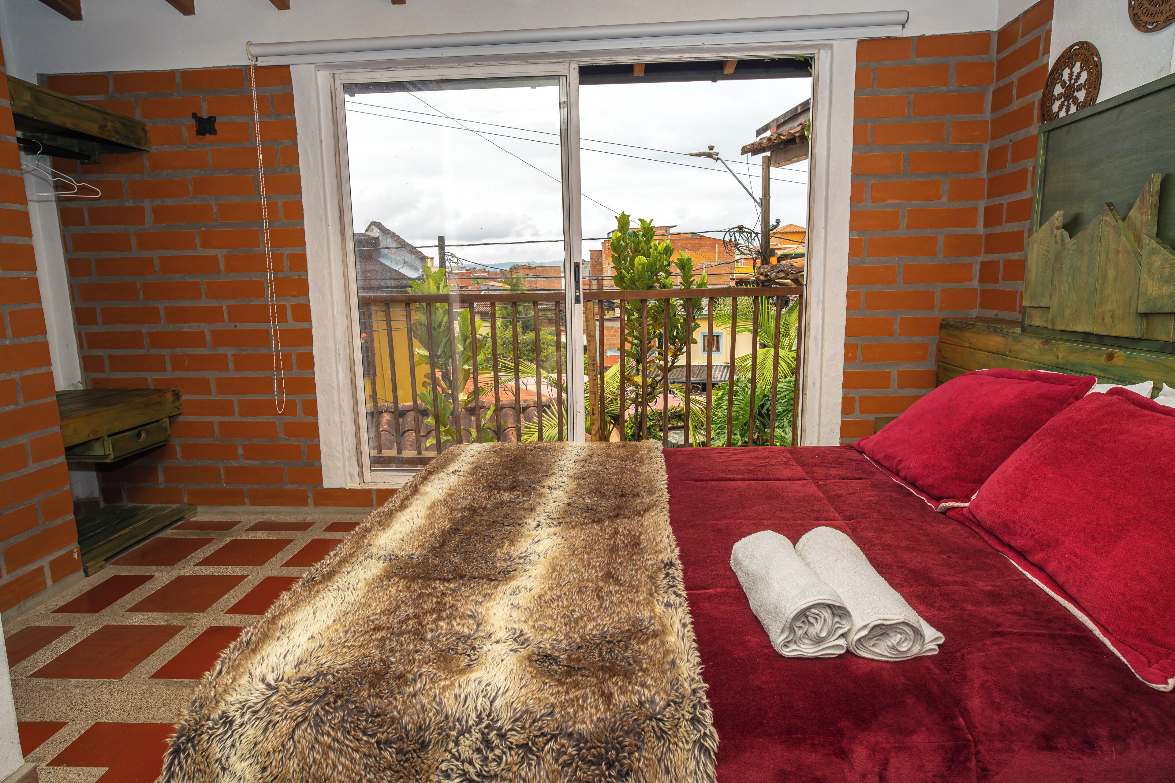 Quarto com cama, manta vermelha e vista por uma porta de vidro.