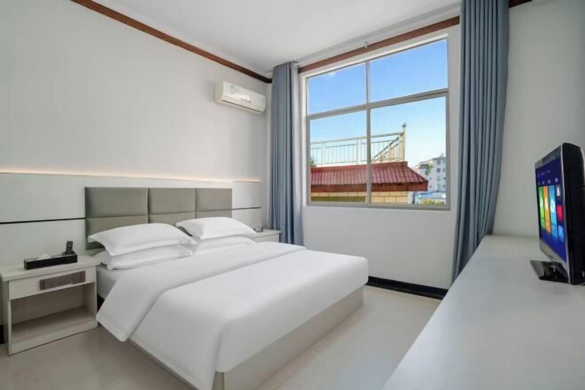 Quarto de hotel moderno com cama grande, mesa de cabeceira, TV e janela com vista para edifícios.