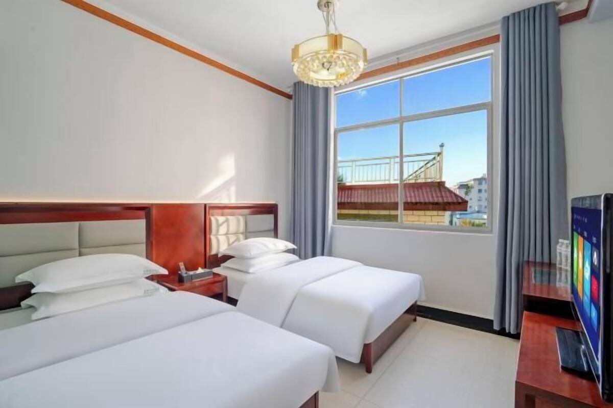 Quarto de hotel com duas camas, televisão, janela com cortinas e um candelabro.
