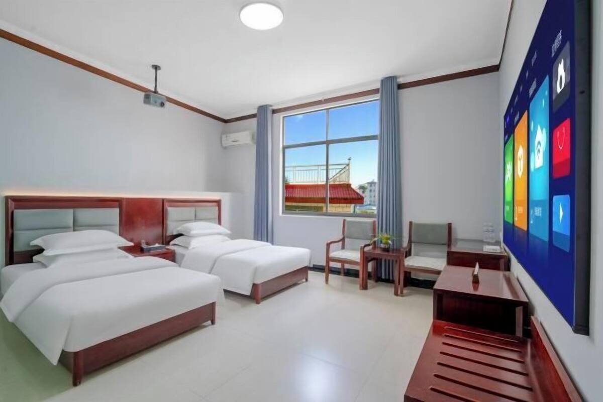 Quarto de hotel com duas camas, uma escrivaninha, uma cadeira, uma televisão e uma grande janela com vista para um edifício.