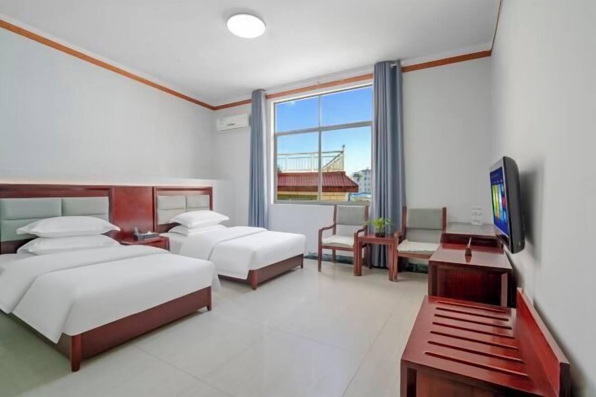 Quarto de hotel com duas camas, televisão, escrivaninha e janela com vista para edifícios.
