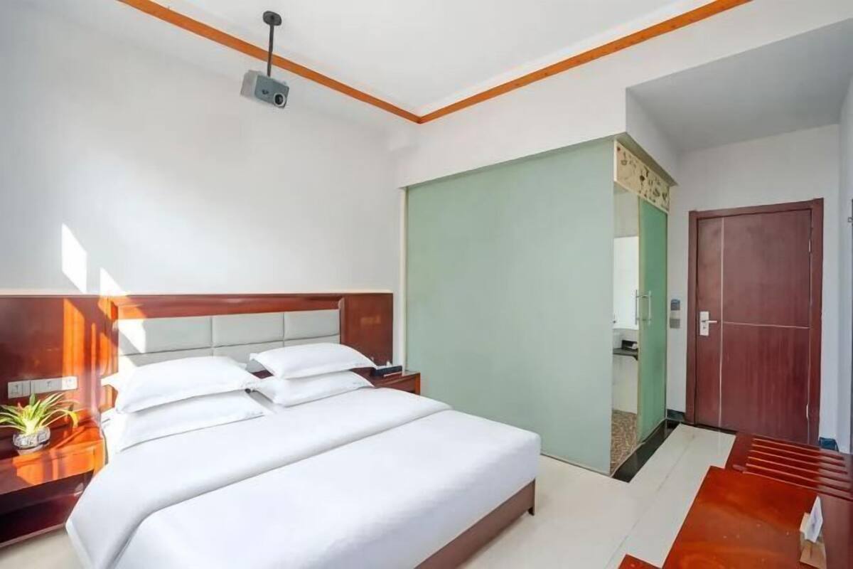 Quarto de hotel com cama, mesas de cabeceira, espelho, porta e projetor no teto.
