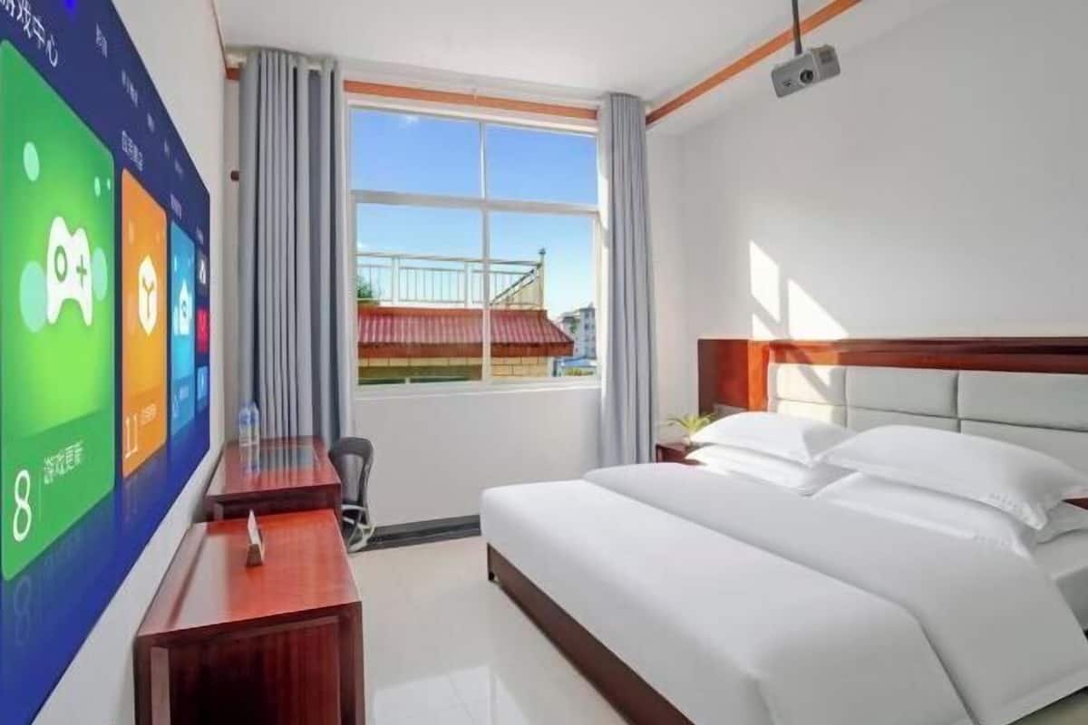 Quarto de hotel com uma televisão grande, uma cama, uma escrivaninha e uma janela com vista para edifícios.