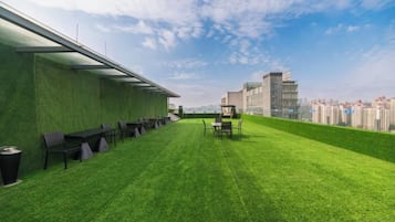 Terraço ao ar livre com gramado verde, área de estar e vista para a paisagem urbana.