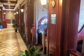 Um corredor de hotel com piso estampado, portas de madeira e plantas em vasos.