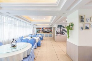 Uma sala de jantar de hotel com mesas redondas, cadeiras azuis e um bar ao fundo.