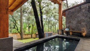 Piscina com muro de pedra e pérgola de madeira, rodeada por árvores.
