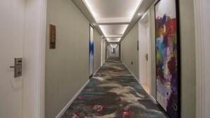 Corredor de hotel com carpete floral, iluminação embutida e um quadro abstrato colorido na parede direita.
