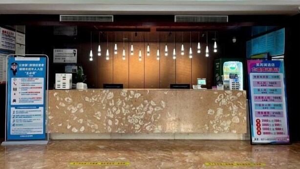 Uma área de recepção de hotel com balcão de mármore, luminárias pendentes e cartazes informativos.