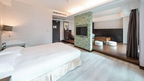 Quarto de hotel moderno com uma cama grande, área de estar com almofadas, televisão e lareira.