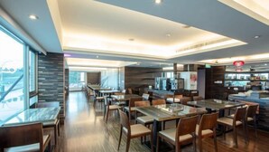 Restaurante moderno com mesas e cadeiras de madeira, um espaço de bar e grandes janelas com vista.
