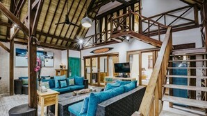 Uma sala de estar espaçosa com teto alto, vigas de madeira, um conjunto de sofás, uma televisão e uma escada.