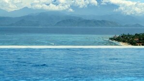 Vista costeira com praia, oceano e montanhas ao fundo.