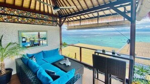 Quarto com vista para a praia, sofá com almofadas azuis, uma mesinha e uma cadeira.