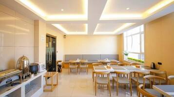 Uma área de refeições moderna com mesas, cadeiras, sistema de buffet e uma grande janela que traz luz natural.