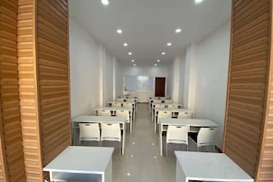 Quarto de hotel com um corredor comprido, várias mesas e cadeiras dispostas para refeições.
