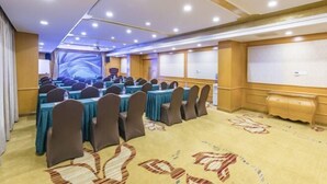 Uma sala de conferências com fileiras de mesas e cadeiras, um palco e uma lousa.
