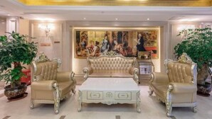 Um lobby luxuoso com uma pintura grande, dois sofás elaborados, uma mesa de centro branca e plantas em vasos.
