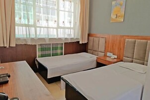 Quarto de hotel com duas camas de solteiro, uma escrivaninha de madeira, uma mesa pequena, uma janela com cortinas e um quadro na parede.