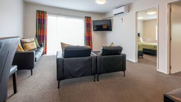 Quarto de hotel moderno com sofá, poltrona, TV de tela plana e cama.