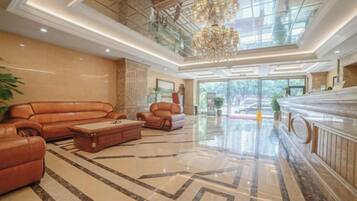 Um hall amplo com teto alto, um candelabro, um sofá de couro, uma mesa de centro e piso de mármore.