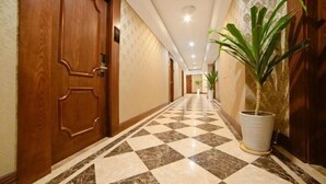 Um corredor de hotel com piso xadrez, portas de madeira e um vaso de planta.