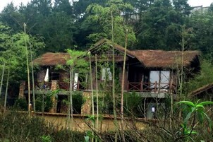 Uma cabana rústica com telhado de palha, rodeada por uma floresta densa.