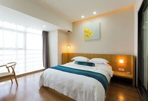 Quarto de hotel com uma cama grande, uma mesinha de cabeceira de madeira, uma cadeira e uma janela com cortinas.