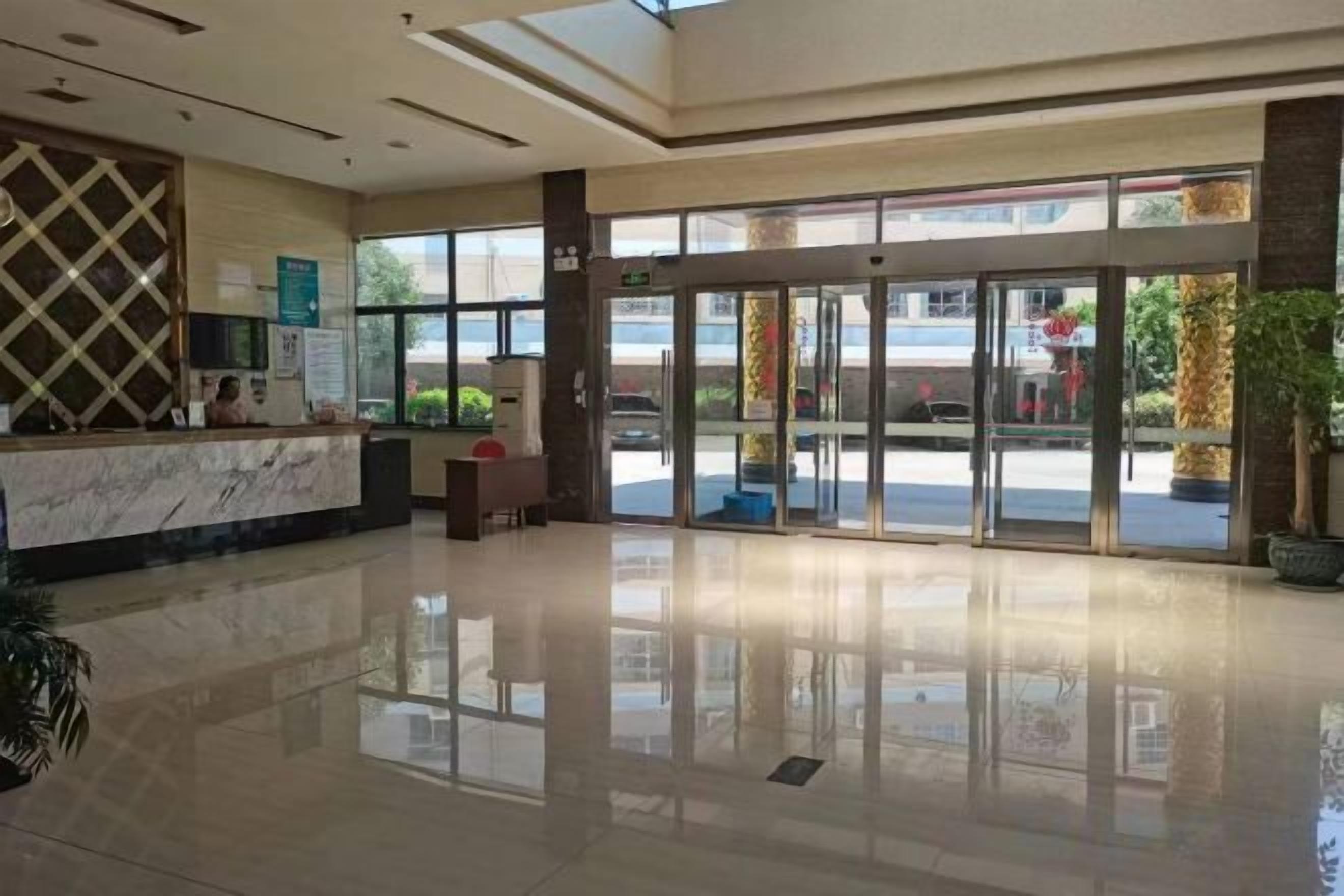 Um saguão de hotel com uma mesa de recepção, porta de vidro e uma grande janela.