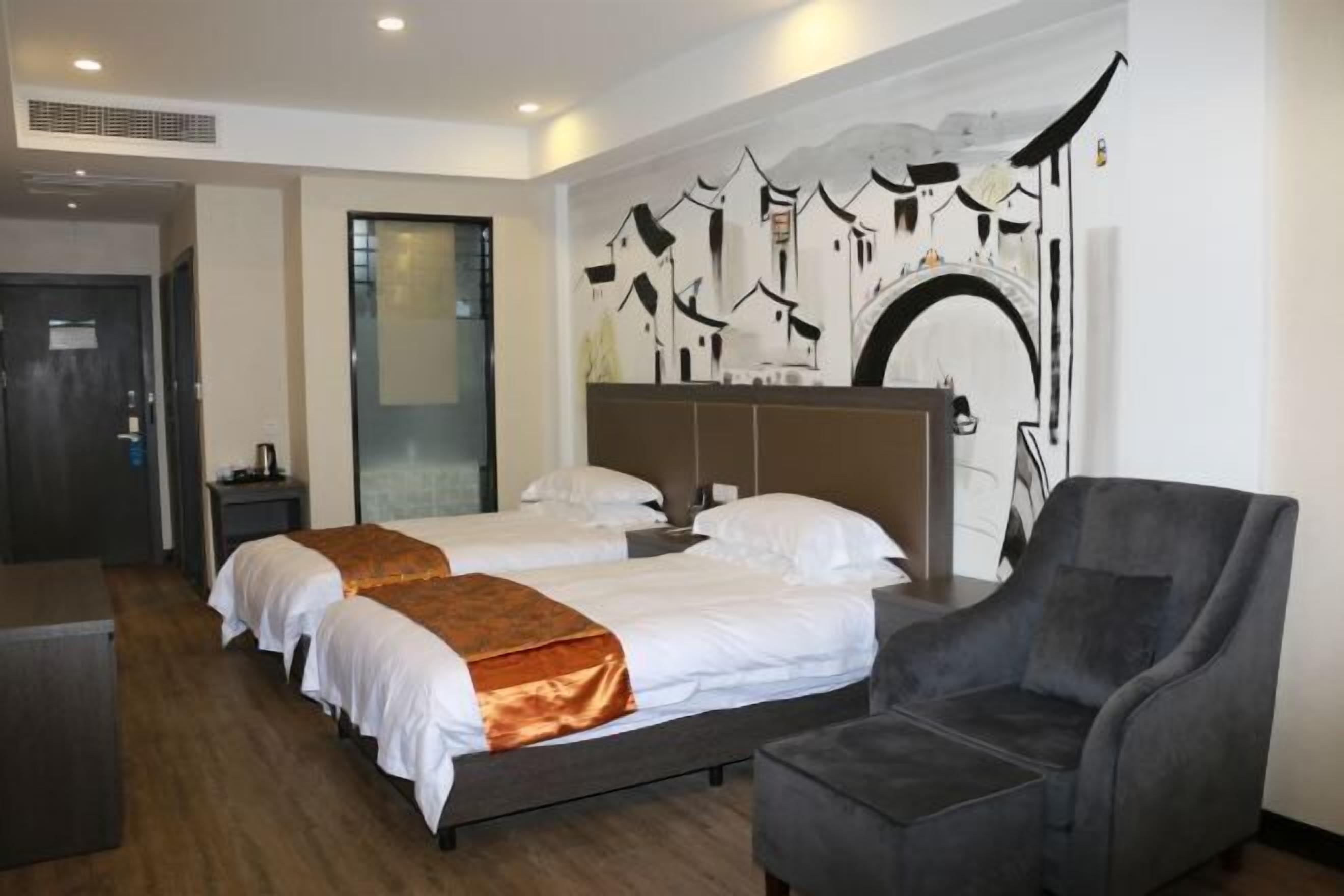 Quarto de hotel com duas camas, uma poltrona cinzenta e um mural grande na parede.