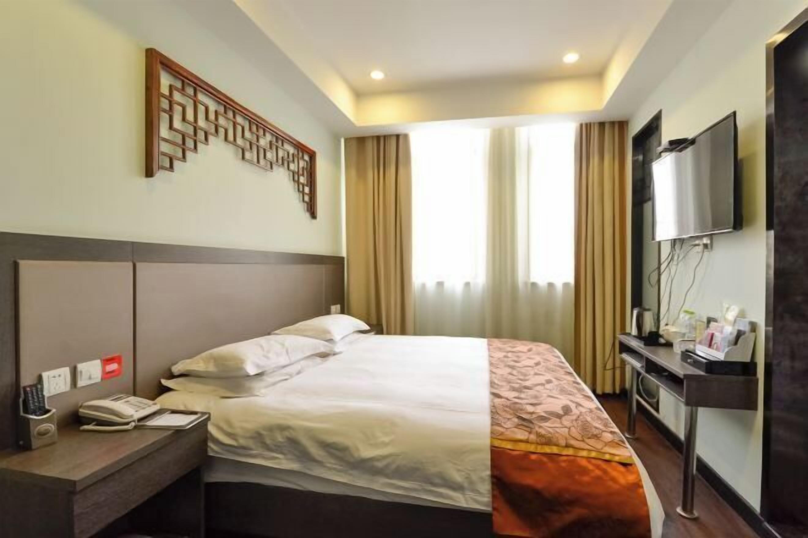 Quarto de hotel com cama, mesa de cabeceira, televisão e cortinas.