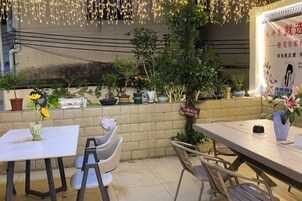 Uma área de refeições ao ar livre com parede de tijolos, plantas em vasos e uma mesa com cadeiras.